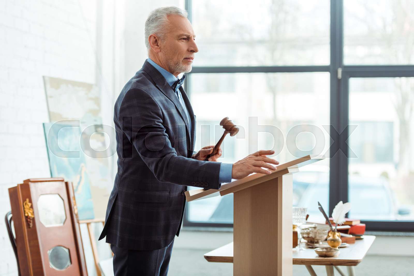 side view of auctioneer holding wooden gavel and looking away during ...
