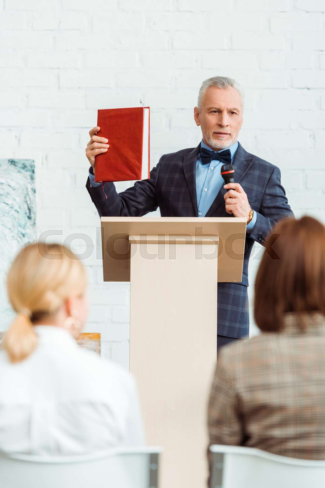 selective focus of auctioneer talking with microphone and holding book ...