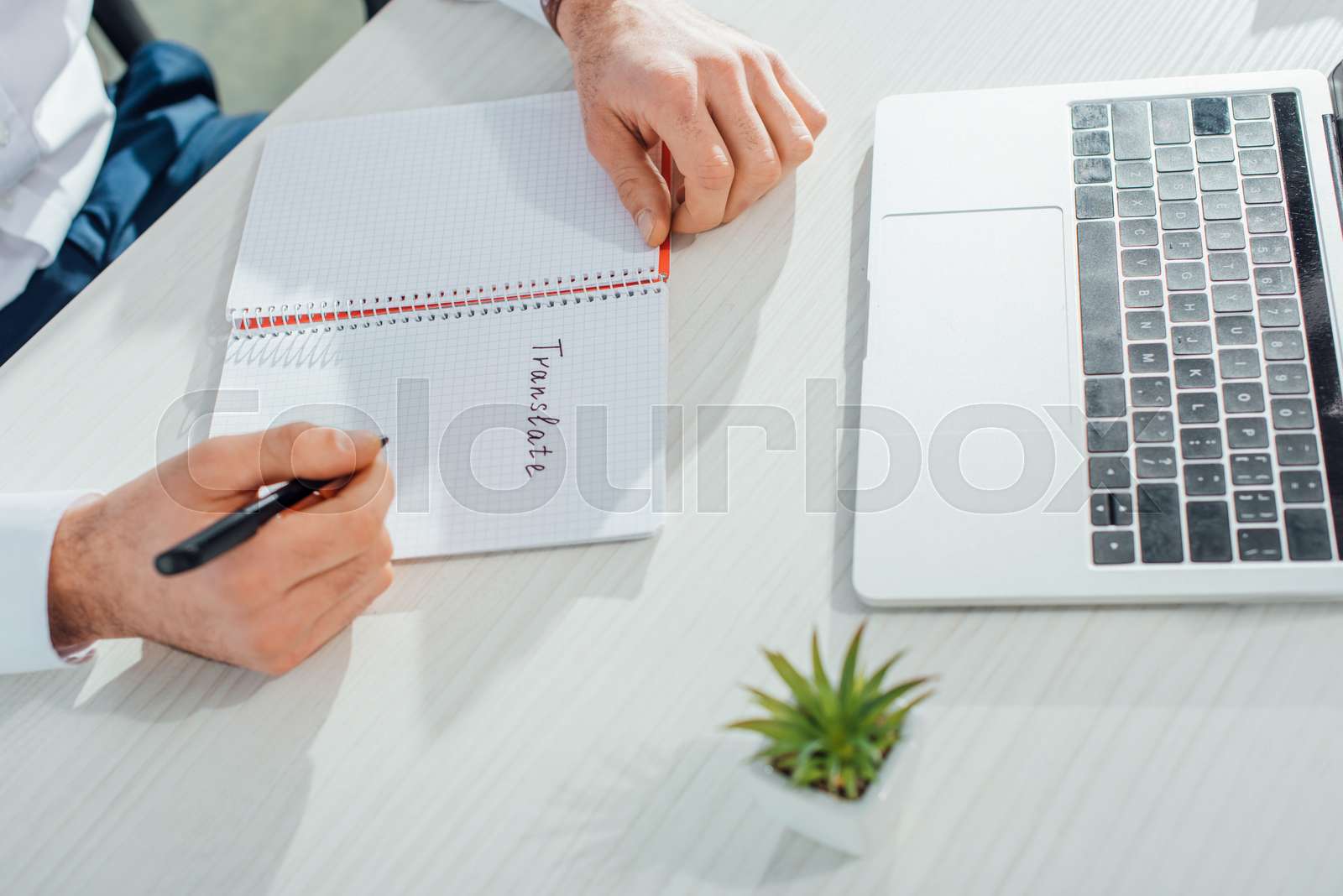 partial view of translator writing in notepad in office with laptop and ...