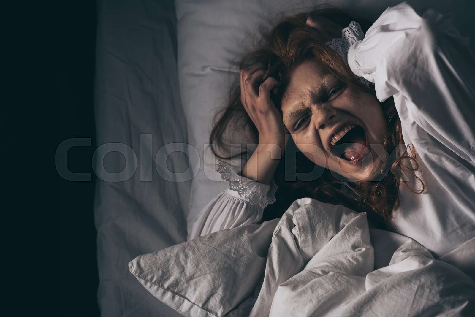top view of obsessed girl in nightgown screaming while lying in bed ...