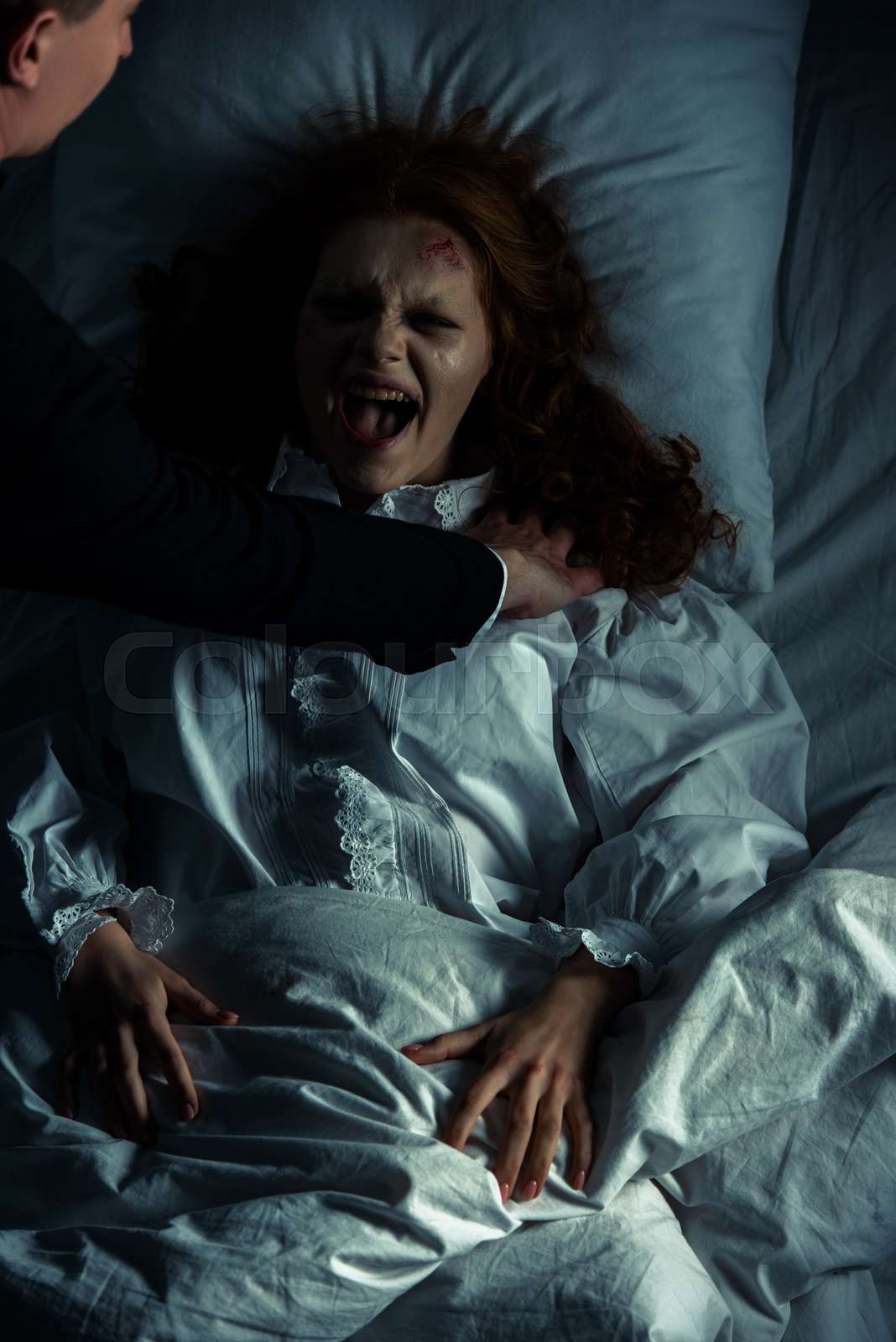 exorcist holding yelling female demon in bed | Stock image | Colourbox