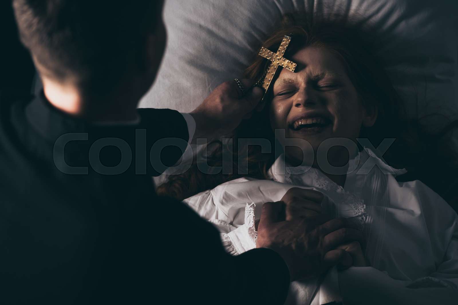 exorcist holding cross over laughing demon in bed | Stock image | Colourbox