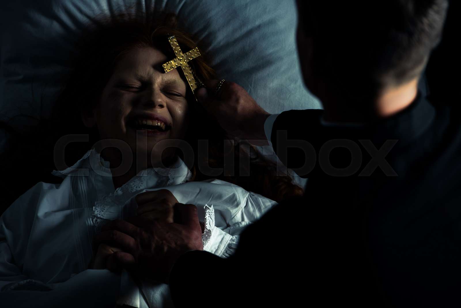 exorcist holding cross over laughing demon in bed | Stock image | Colourbox