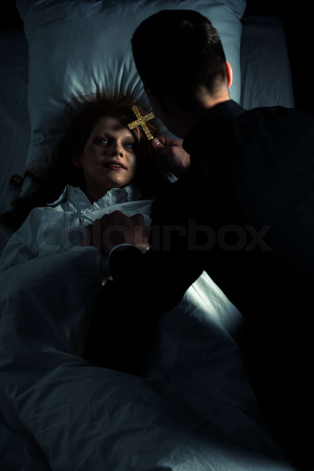 exorcist holding cross over female creepy demon in bed | Stock image ...