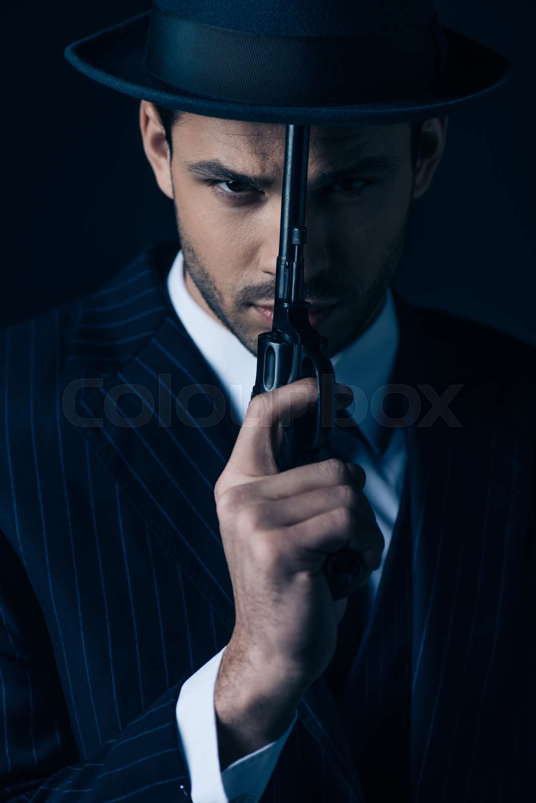 Gangster holding gun in front of face on dark blue | Stock image ...