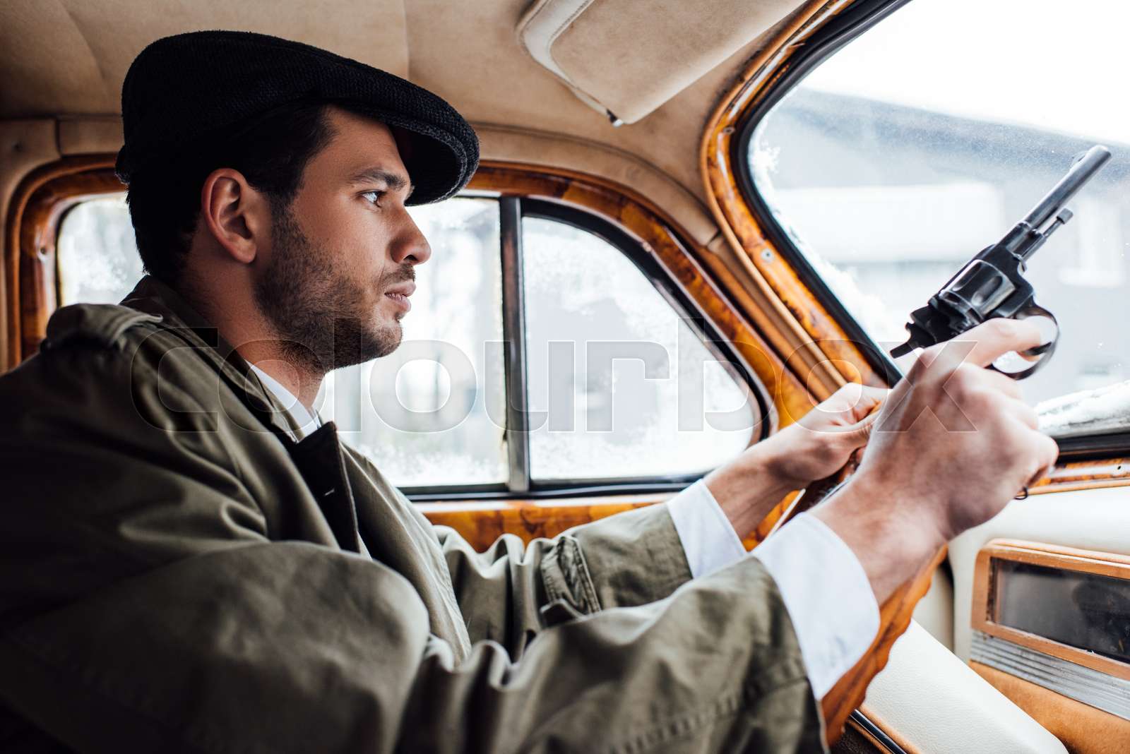Selective focus of gangster in flat cap and coat with gun driving car ...