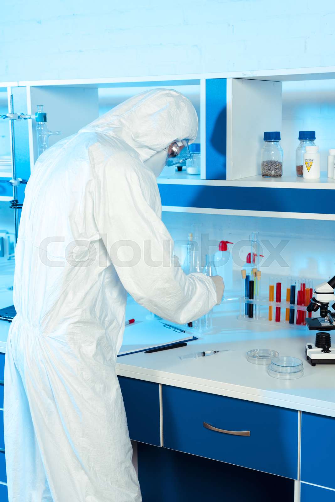 scientist in hazmat suit standing near syringe, clipboard and ...
