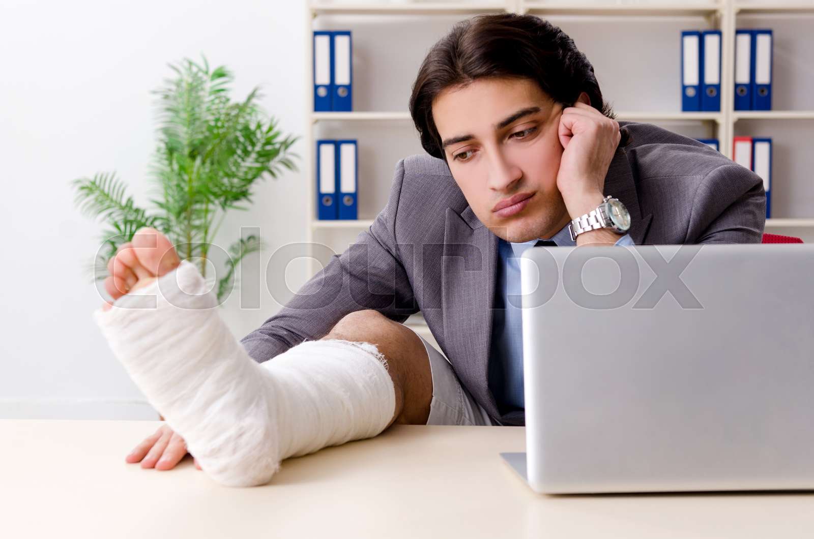 Leg injured employee working in the office | Stock image | Colourbox