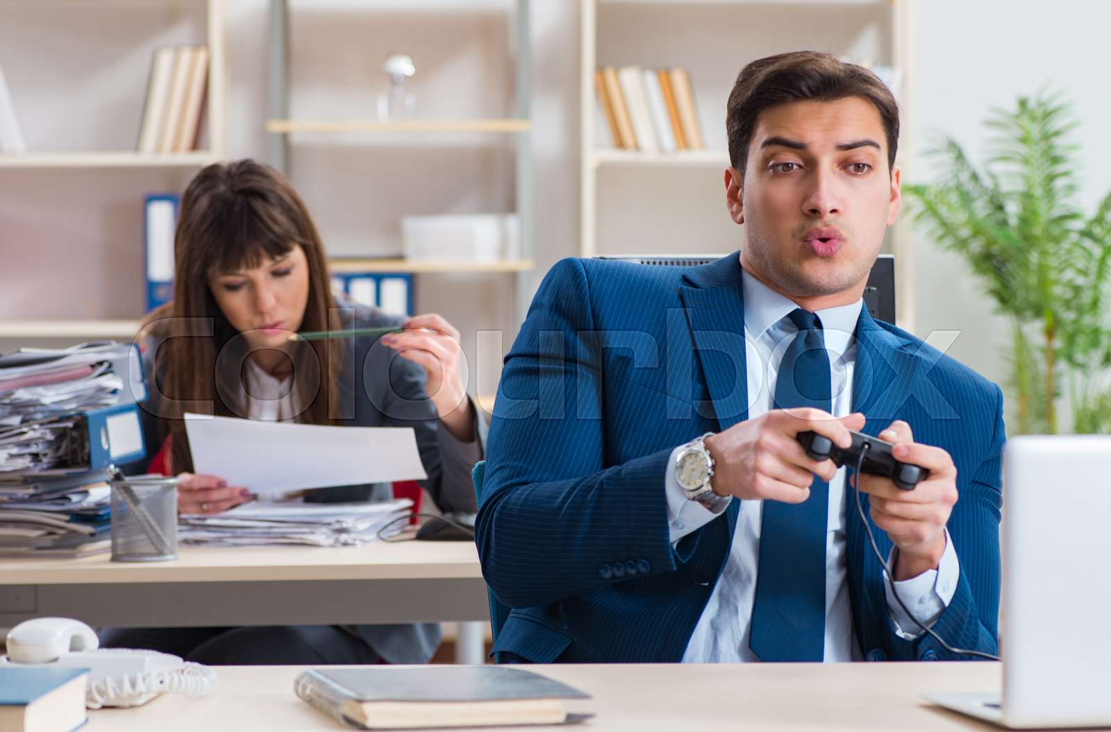 Man playing games in office while colleague is busy | Stock image ...