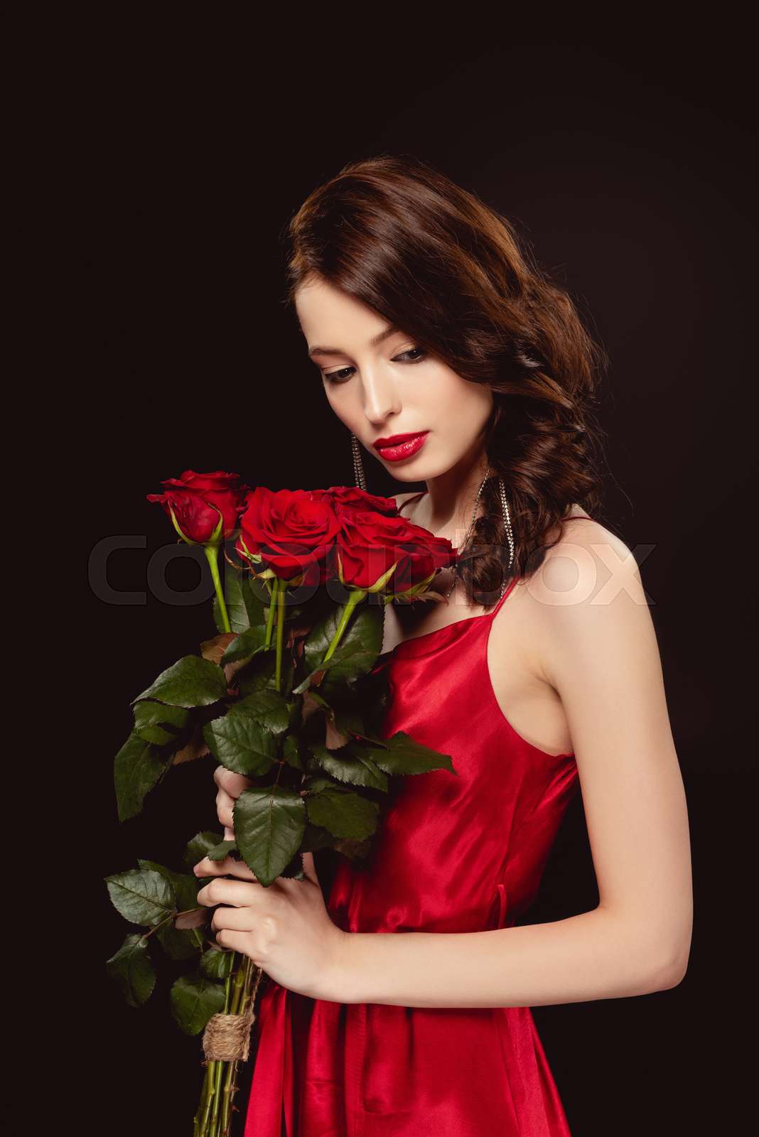 Beautiful woman in red dress holding bouquet of roses isolated on black ...
