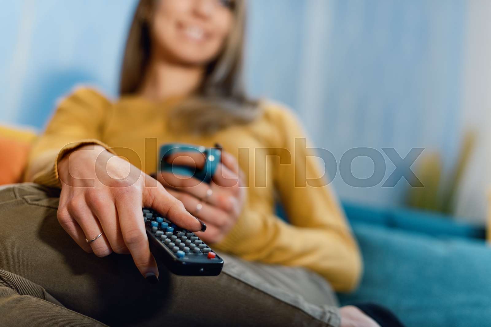 Woman holding a remote control and watching TV | Stock image | Colourbox
