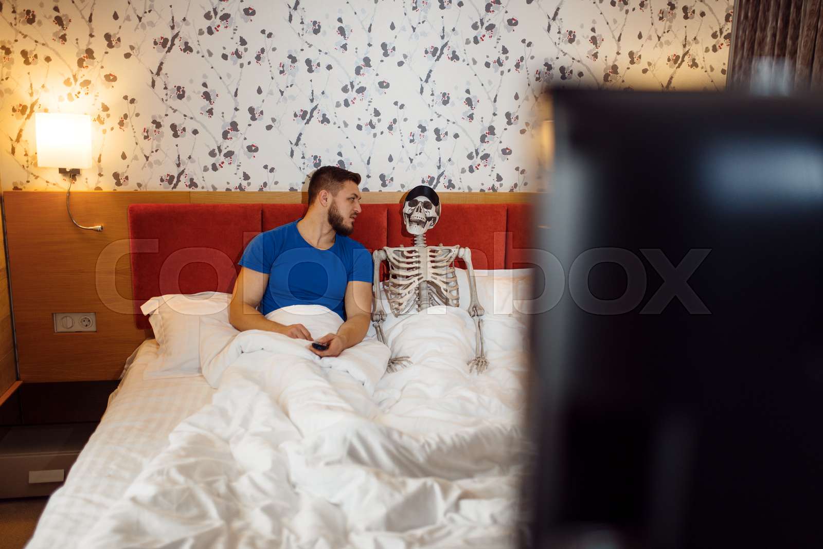 Man and human skeleton watching TV in the bed | Stock image | Colourbox