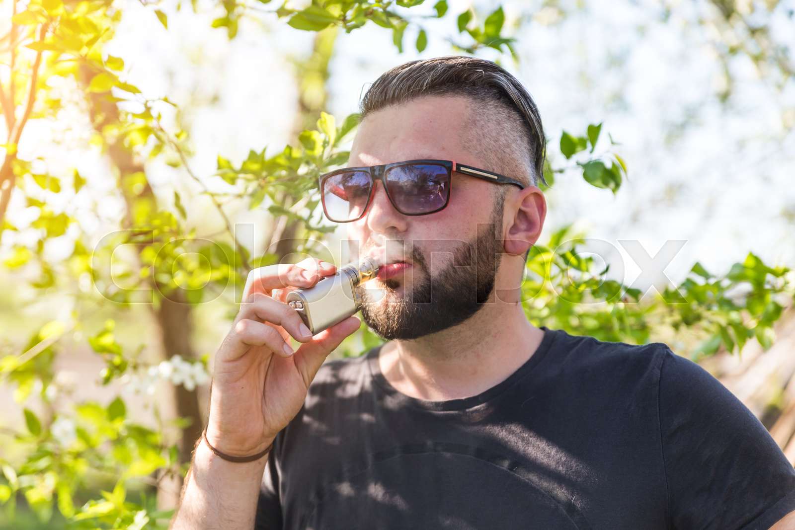 Portrait of young guy with beard vaping an electronic cigarette with ...
