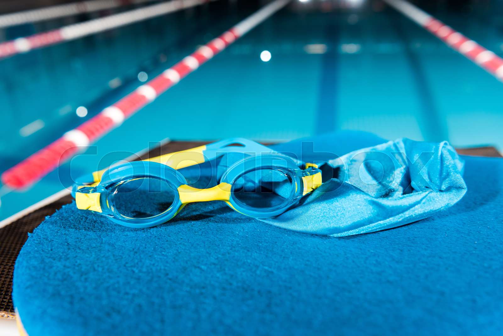 goggles and swimming cap on flutter board near swimming pool with blue ...