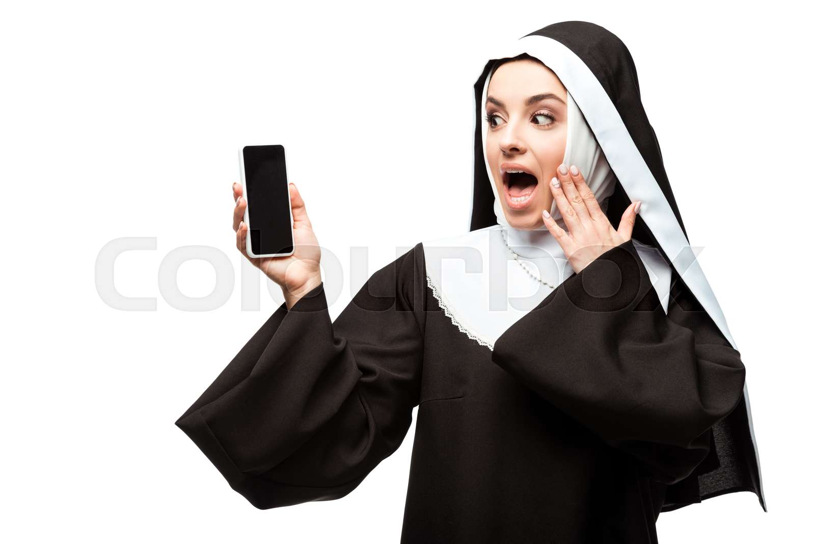 surprised nun presenting smartphone with blank screen isolated on white ...