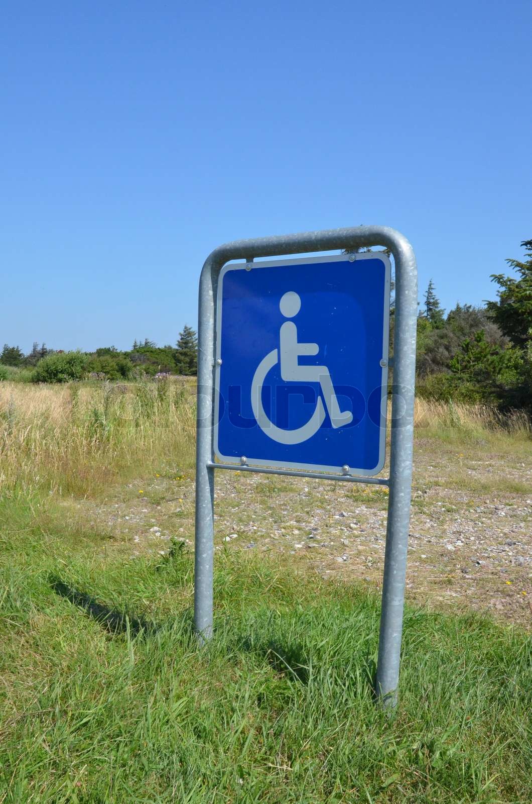 blåt handicap skilt med person i rulle stol ud i naturen i græs og sand ...