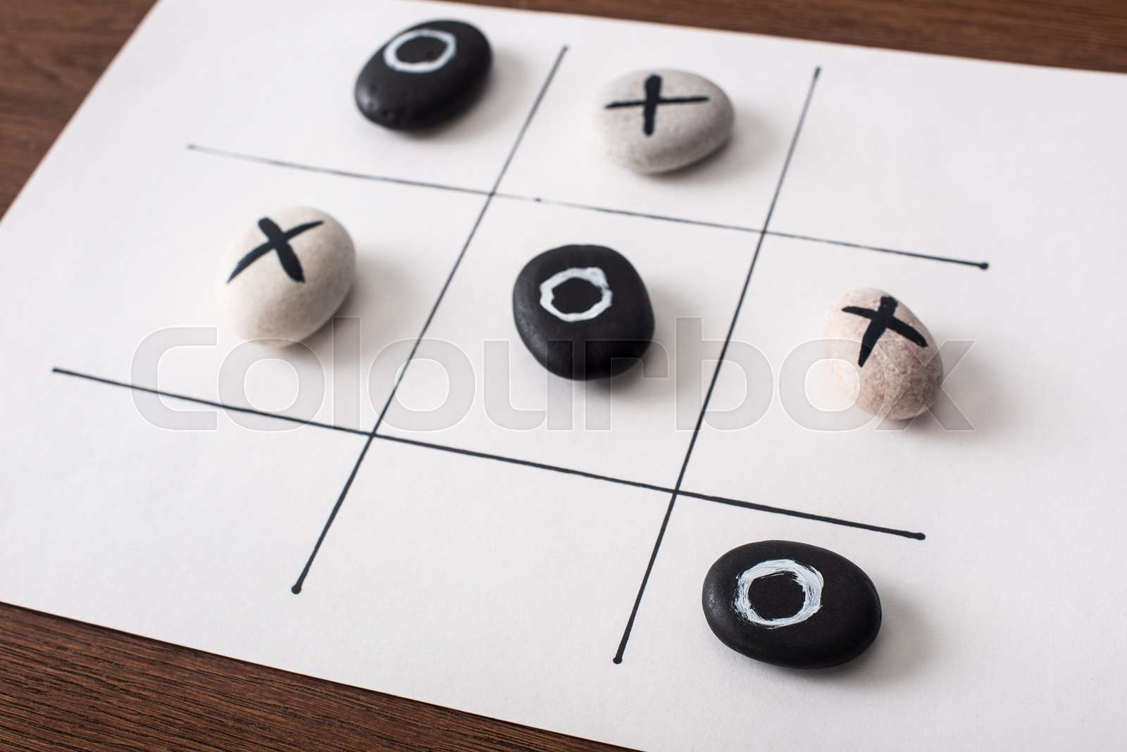 tic tac toe game on white paper with pebbles marked with naughts and ...