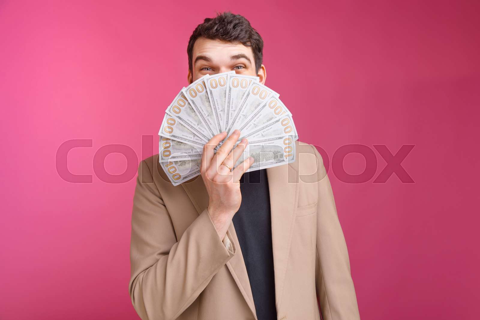 Happy bearded man is covering his face with a bunch of dollars and ...
