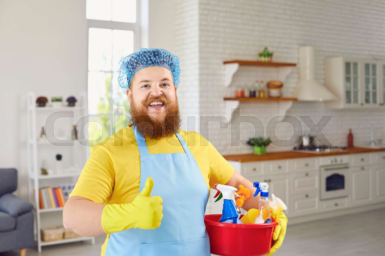 Funny fat man with a beard in an apron cleans the room in the house ...