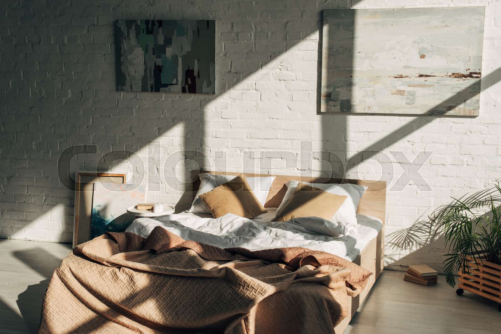 bedroom interior with bed, pillows and paintings in sunlight with ...