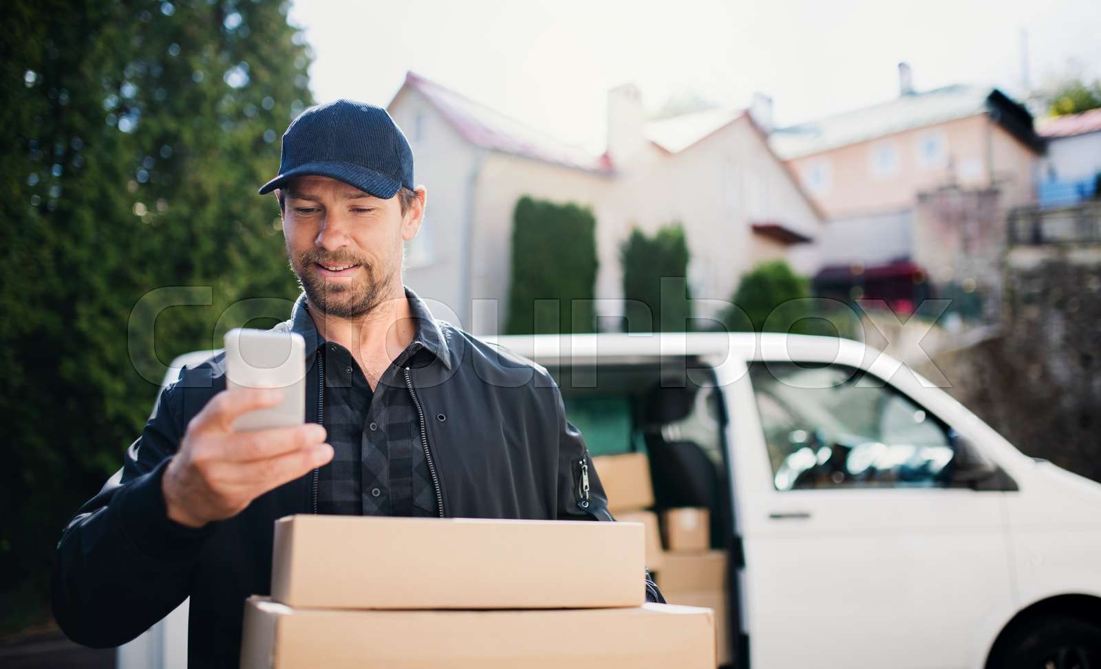 Delivery man courier delivering parcel box in town using smartphone ...
