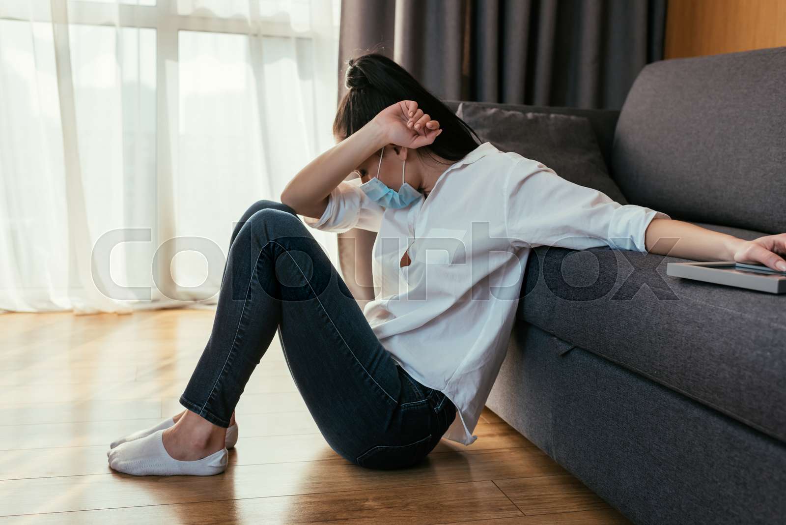 grieving young woman in medical mask obscuring face with hand while ...