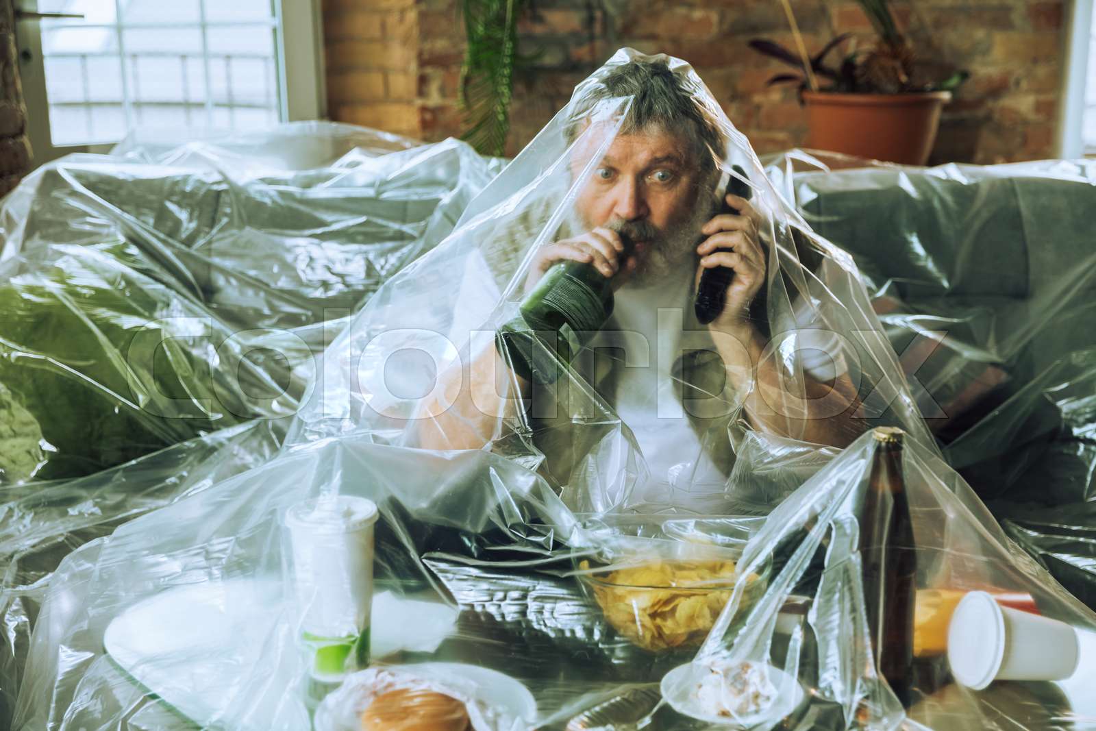 Senior man covered with plastic, eating fast food and drinking beer ...