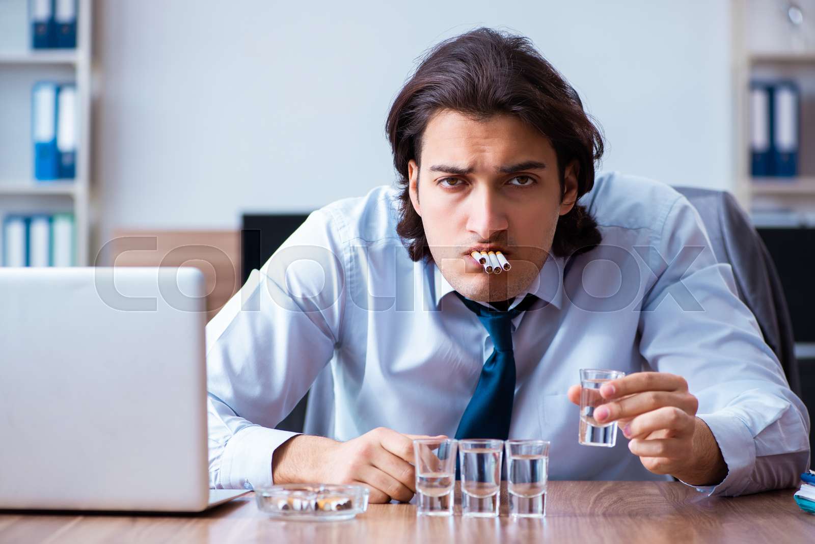 Male employee drinking vodka and smoking cigarettes at workplace ...