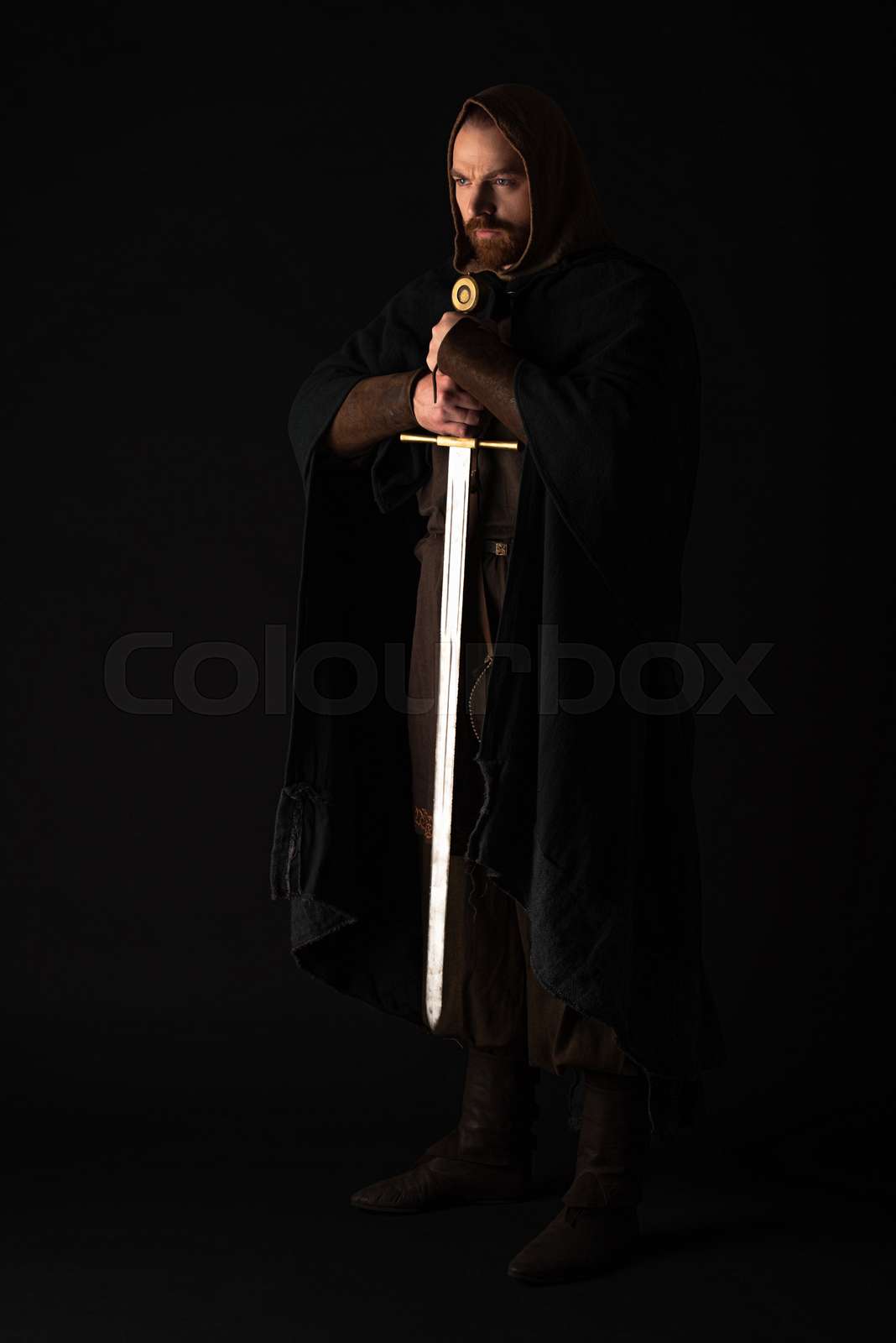 medieval Scottish man in mantel with sword in dark isolated on black ...