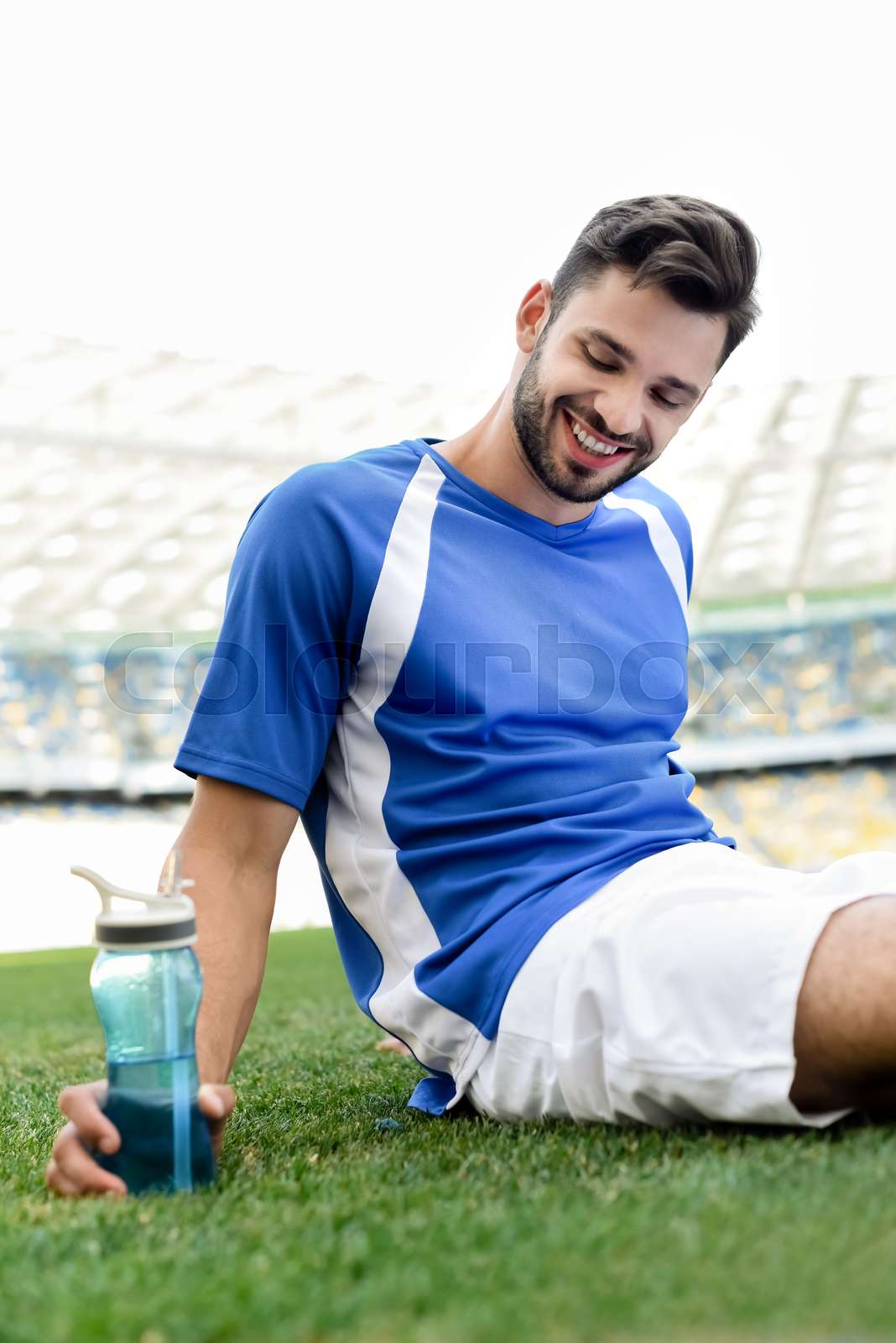 smiling professional soccer player in blue and white uniform sitting on ...