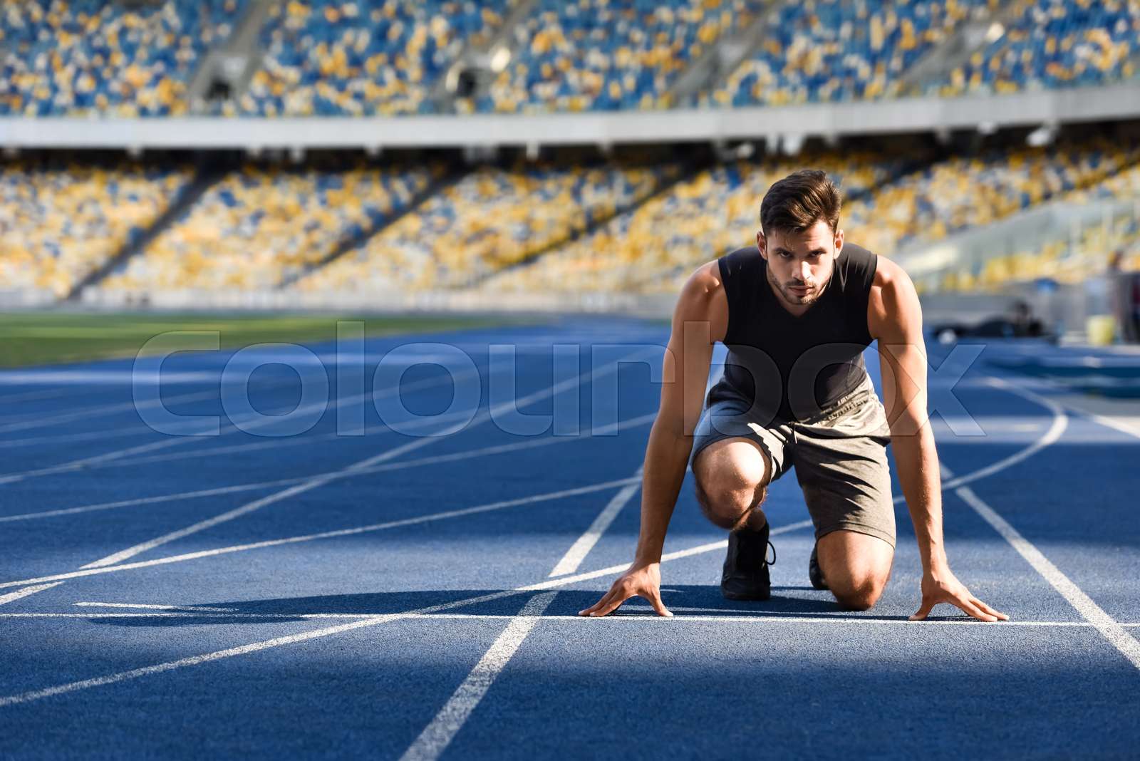 handsome runner in start position on running track at stadium | Stock ...