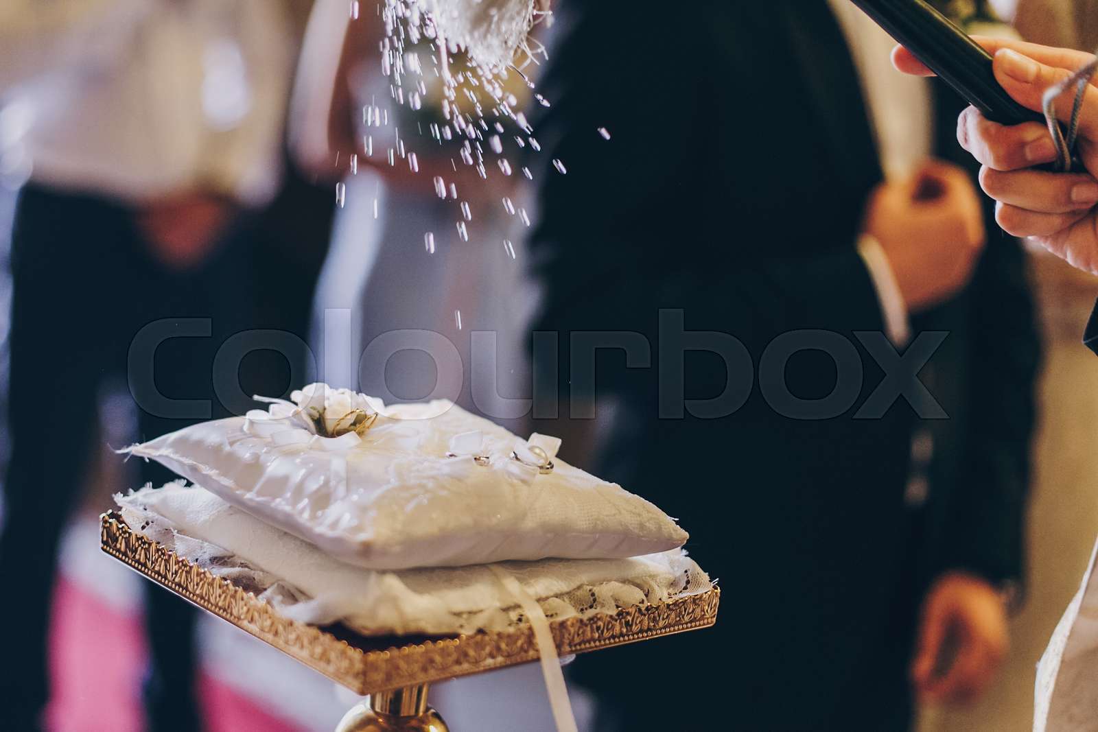 Priest blessing silver wedding rings on silk pillow with holy water for ...