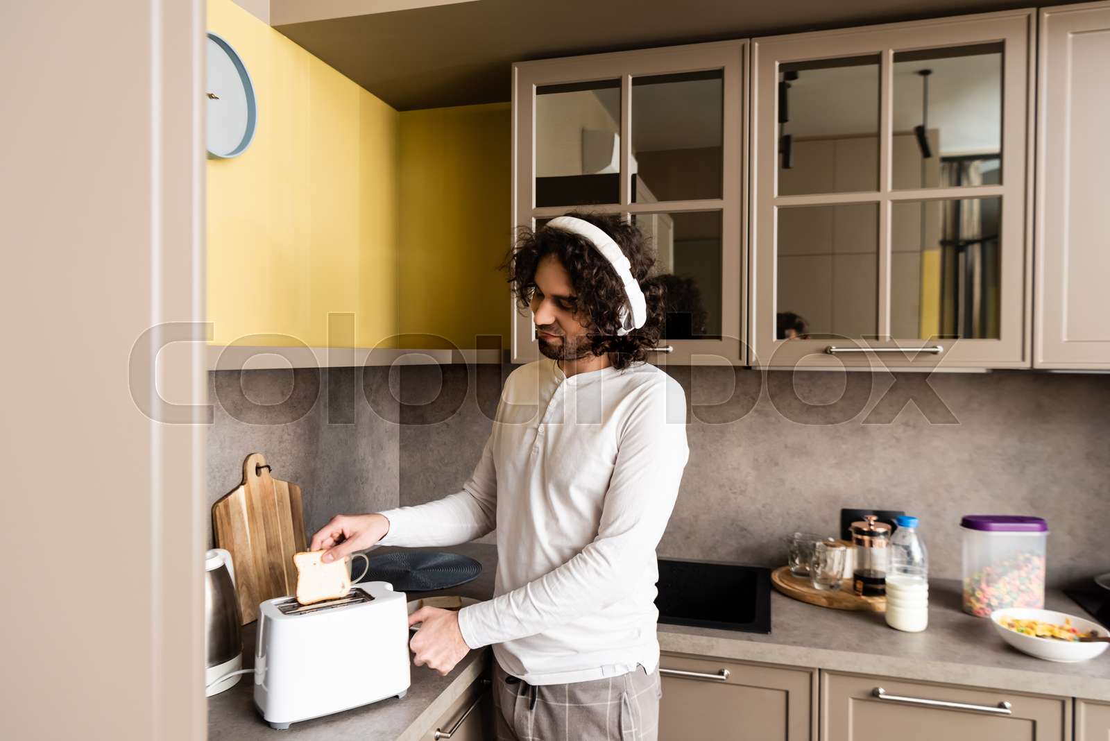 curly man in wireless headphones putting bread into toaster while ...