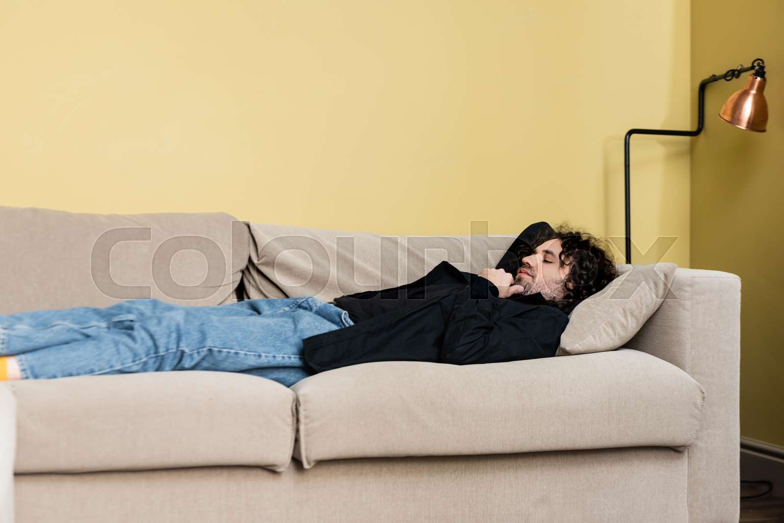 Side view of man lying on couch in living room | Stock image | Colourbox