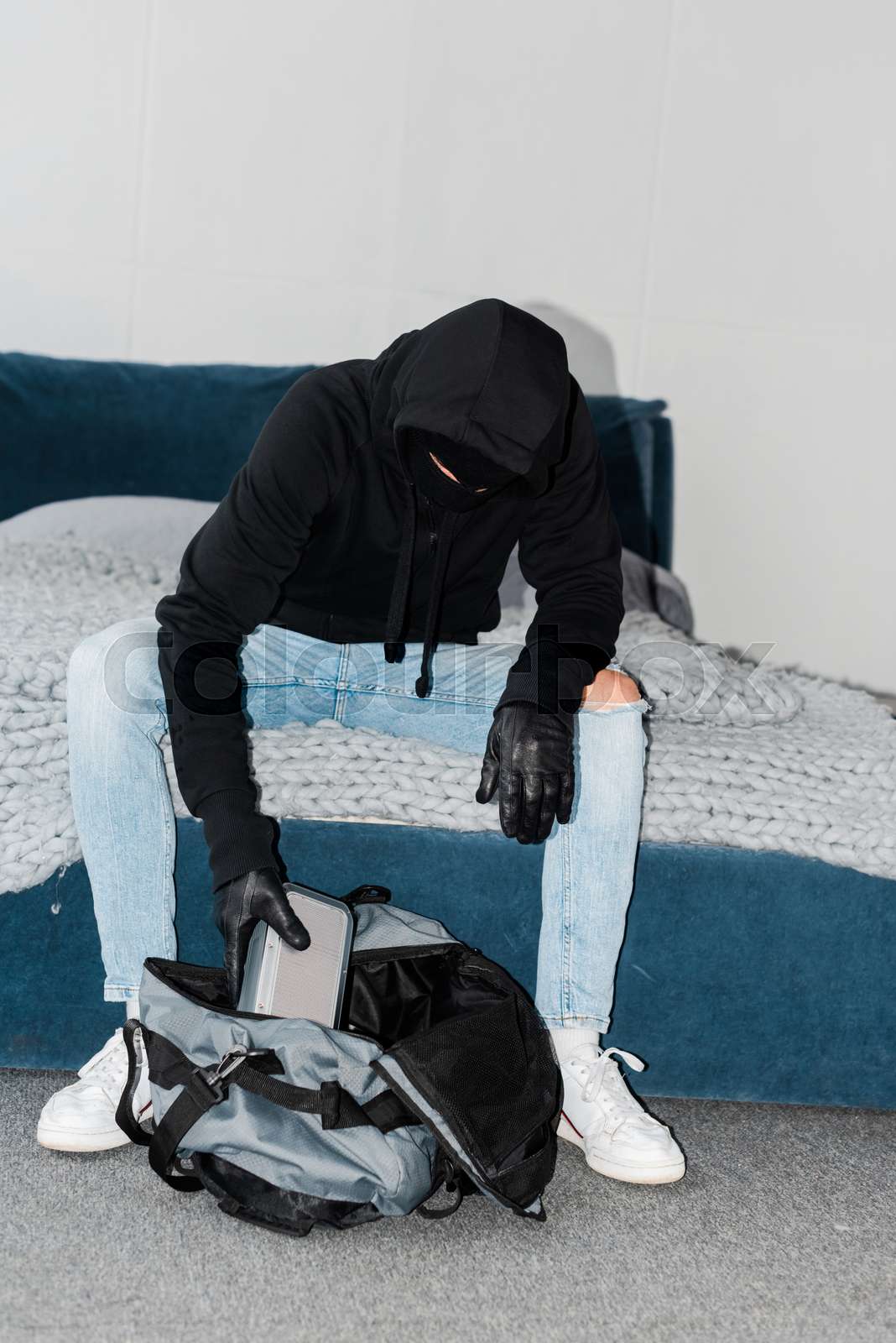 Robber in mask and leather gloves putting wireless speaker in bag on ...