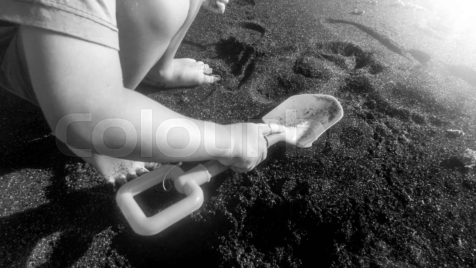 Closeup black and white image of little boy digging sand with toy ...