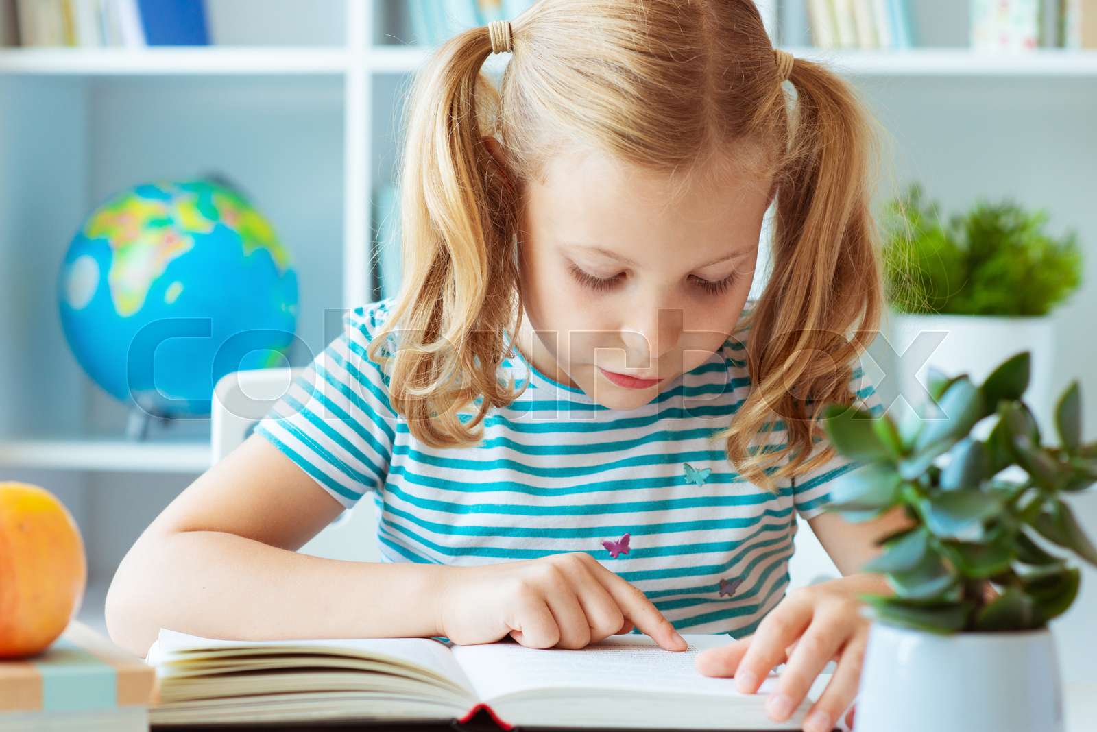 Portrait of a cute little girl read book at the table in classroom ...