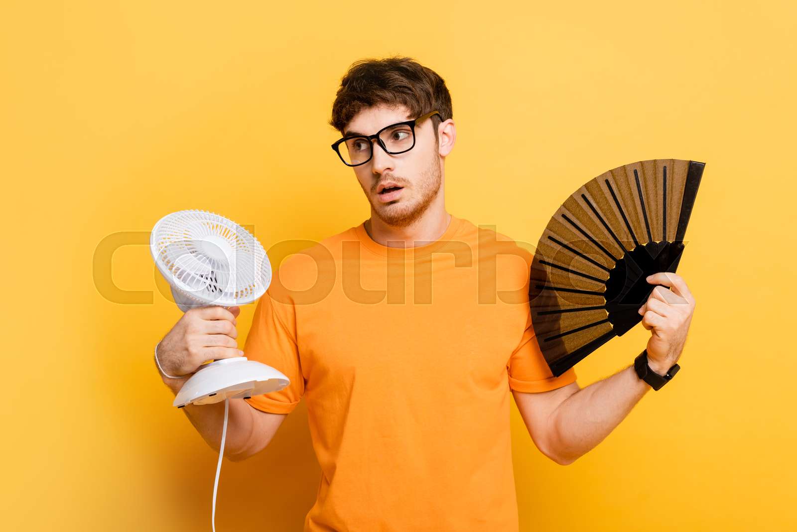 displeased man holding electric and hand fans while suffering from heat ...