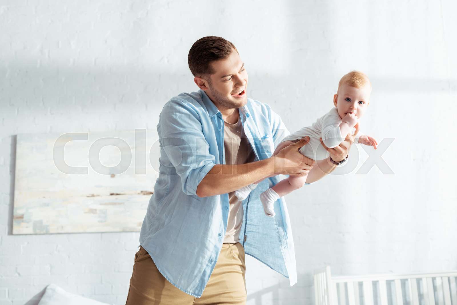 excited young man holding baby in outstretched hands in bedroom | Stock ...