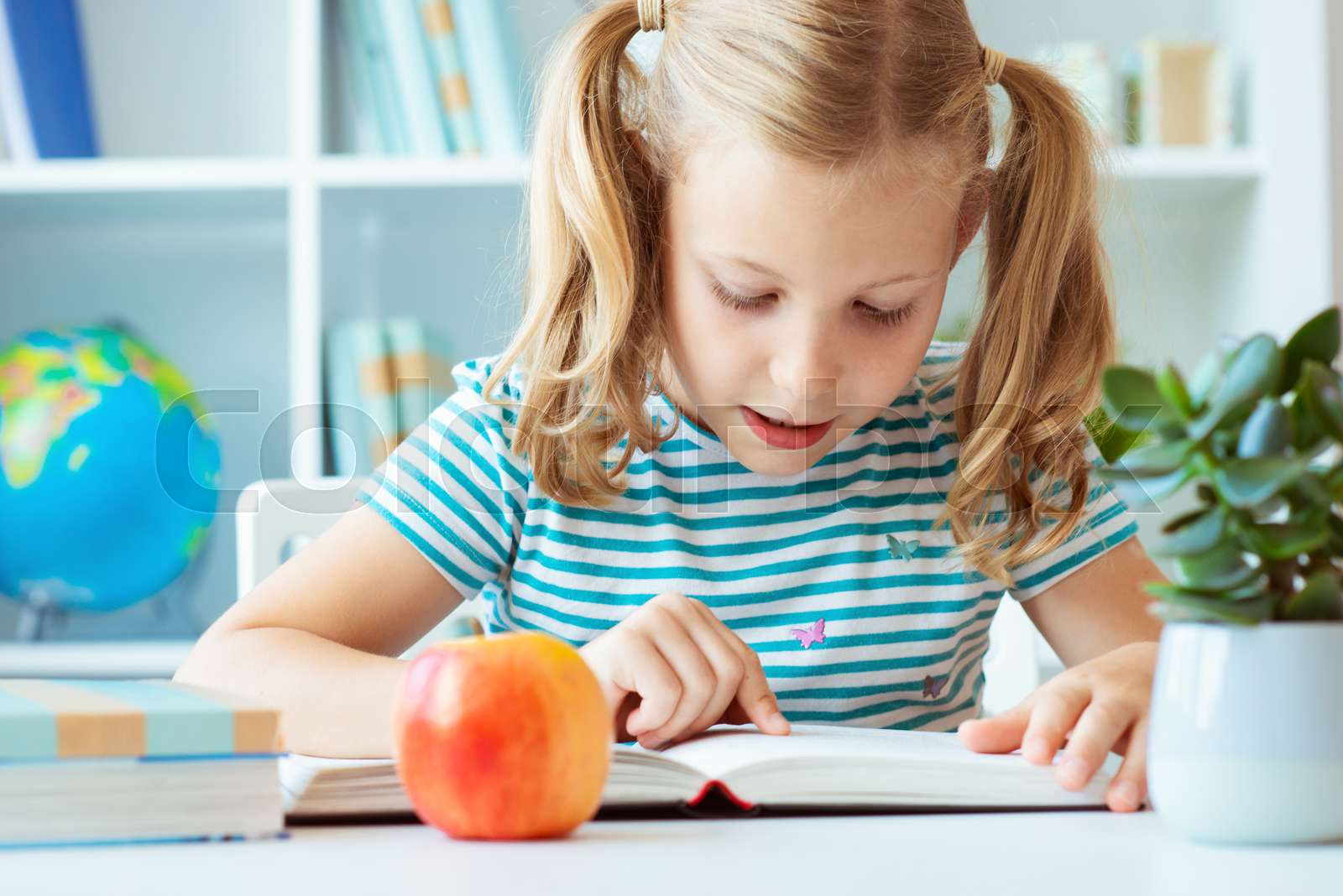 Portrait of a cute little girl read book at the table in classroom ...