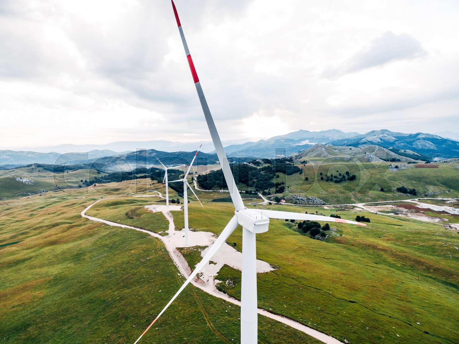 A drone flies among huge bursts of wind turbines at a wind farm in ...