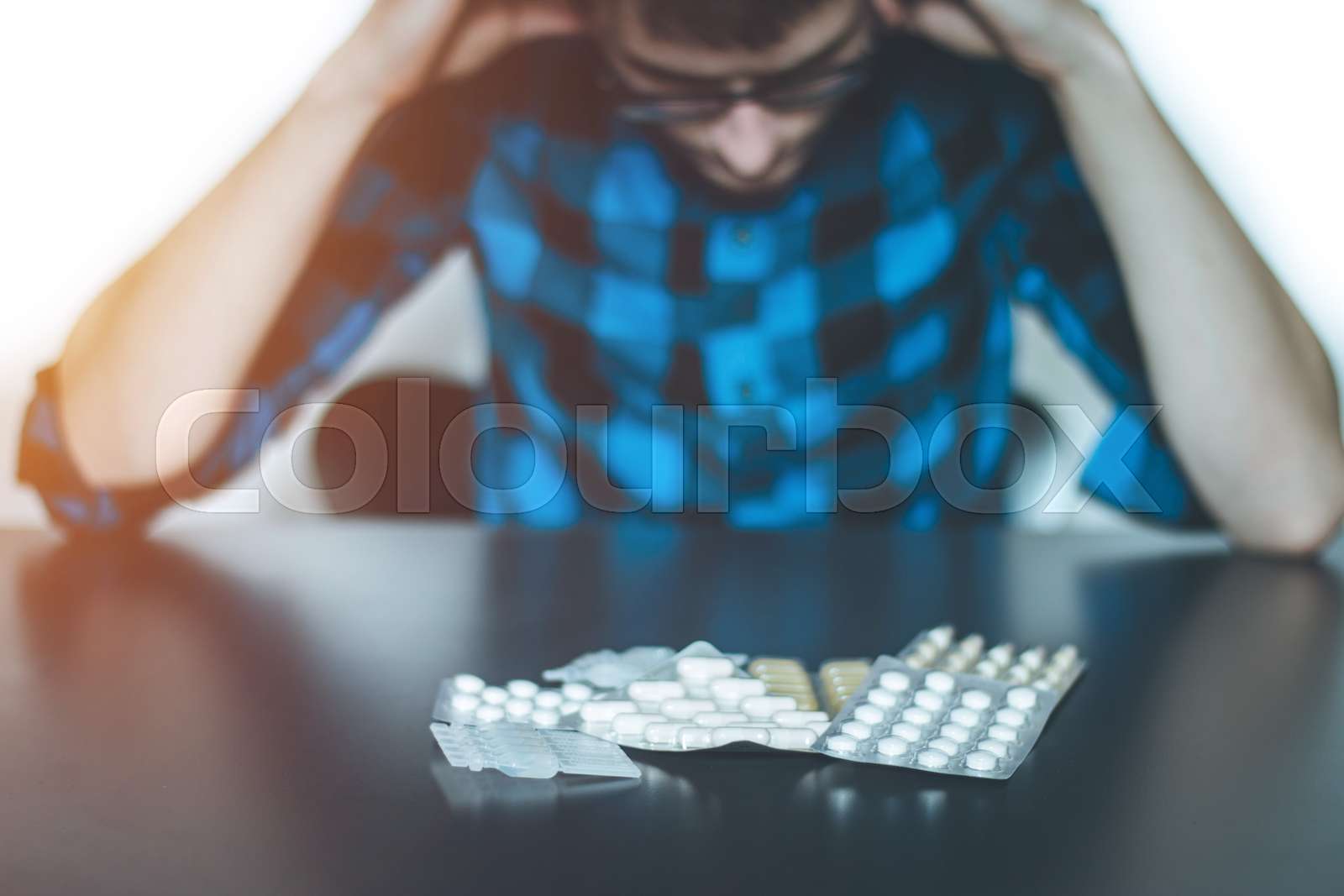 Depressed man taking drugs. Young man sitting on a table, drugs and ...