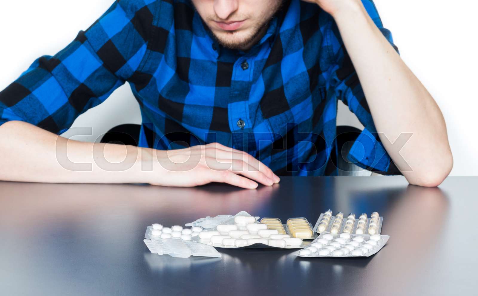Depressed man taking drugs. Young man sitting on a table, drugs and ...