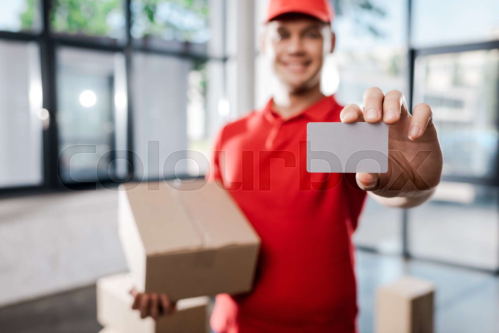 selective focus of happy delivery man in cap holding blank card and ...