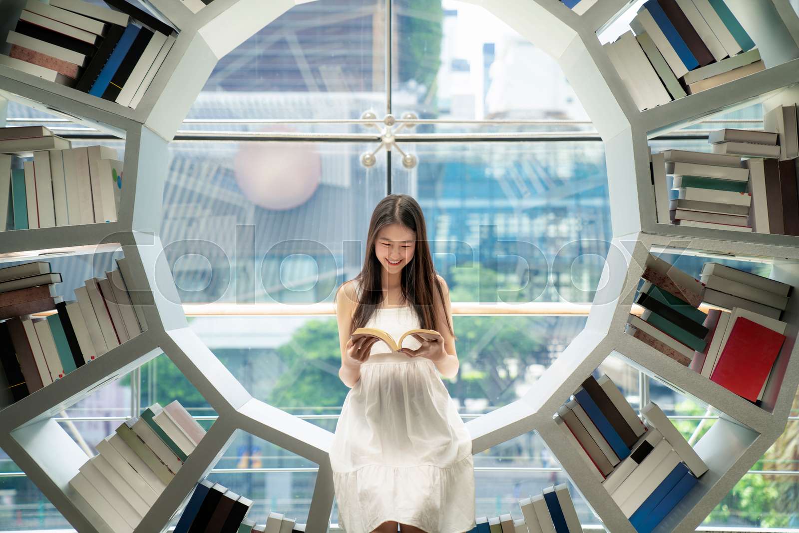 Asian girl reading on a bookshelf in a library | Stock image | Colourbox