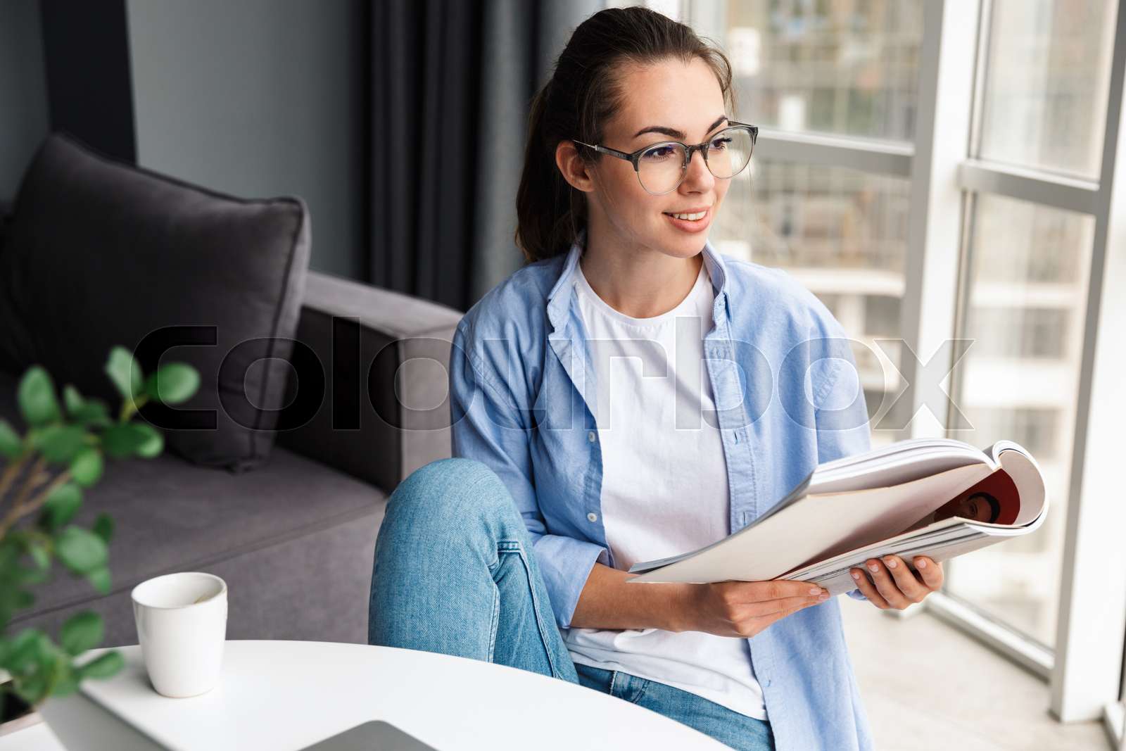 Image of woman reading book and working with laptop while sitting ...
