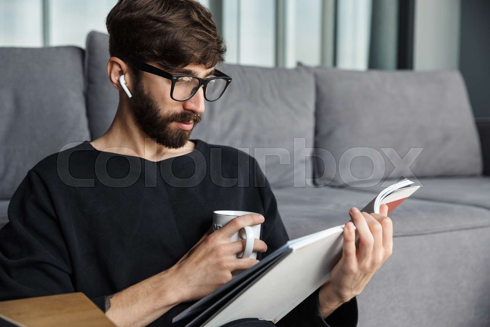 Image of focused man drinking coffee and reading magazine while sitting ...