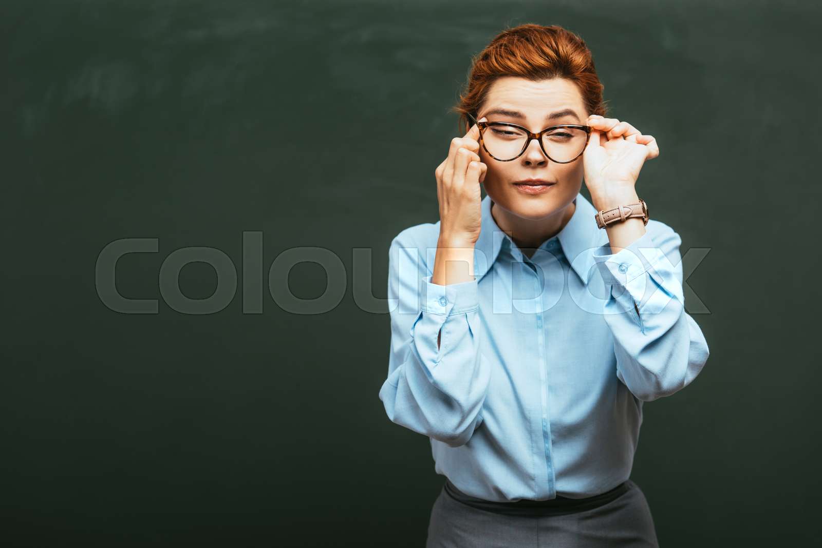 young teacher touching eyeglasses and eye while standing near ...