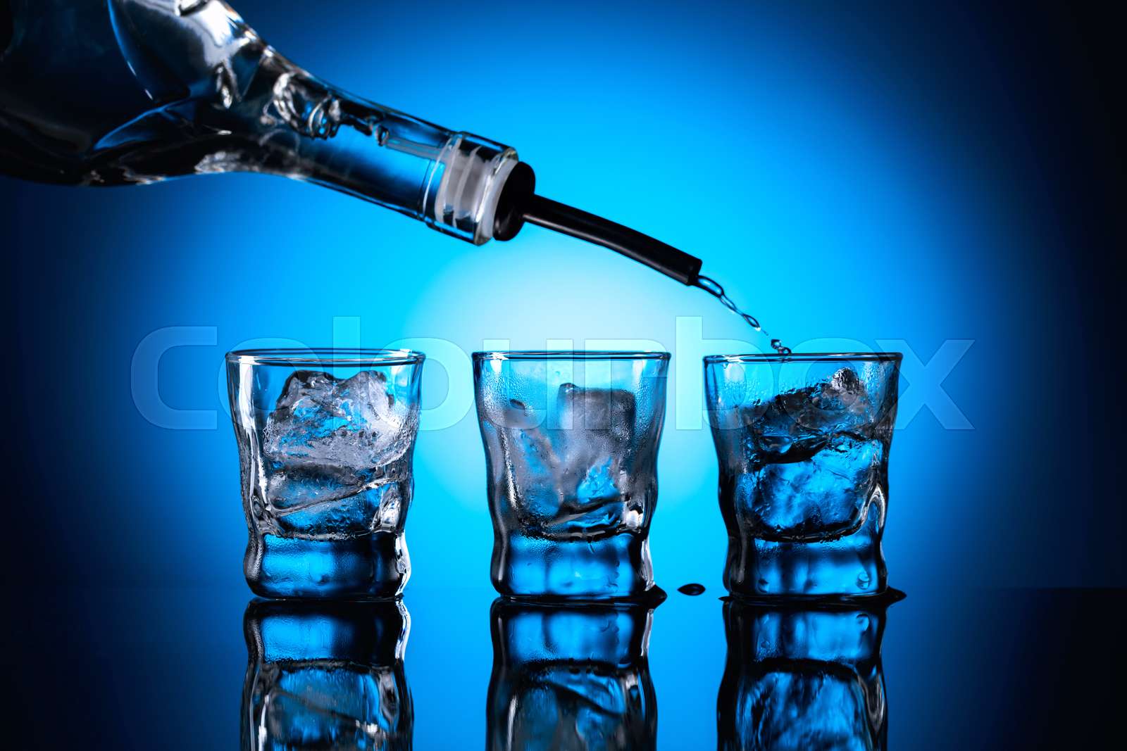 Vodka is poured from bottle into glasses with ice. | Stock image ...