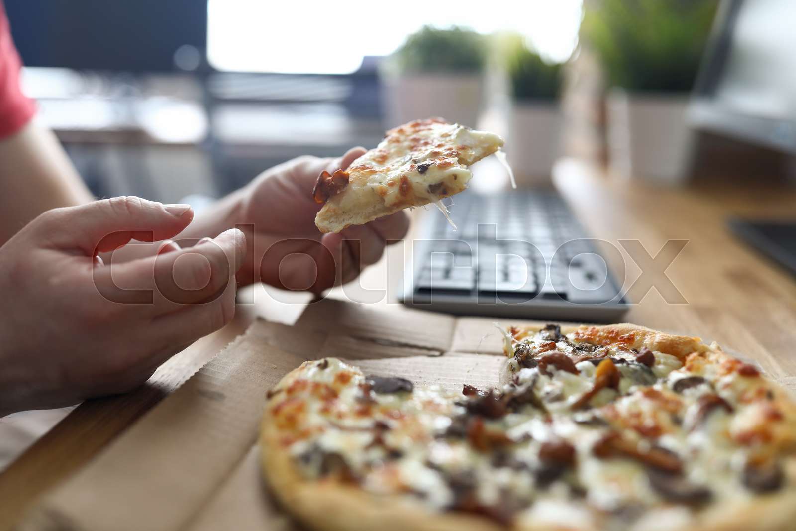 Man eating pizza in workplace in front computer | Stock image | Colourbox